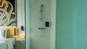 Quarto de hotel com chuveiro, uma cama com travesseiro rotulado "SOCIA TEL", mesa de cabeceira com abajur e uma obra de arte pendurada na parede.