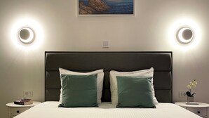 Uma cama bem arrumada com duas almofadas, uma mesinha de cabeceira com um livro e um controle remoto, e um ar condicionado fixado na parede.