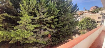 Uma varanda com vista para árvores verdes densas e um prédio com vários andares ao fundo.