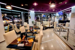 Restaurante com mesas, cadeiras, um suporte para menu e uma tela de televisão.