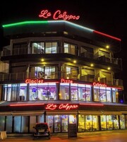Um edifício de vários andares com letreiros iluminados para 'Glacier', 'Pizza' e 'Cafe'.