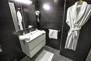Casa de banho moderna com azulejos escuros, toucador branco, secador de cabelo e roupeão pendurado na parede.