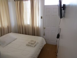 Quarto com cama, cortinas, porta e televisão presa à parede.