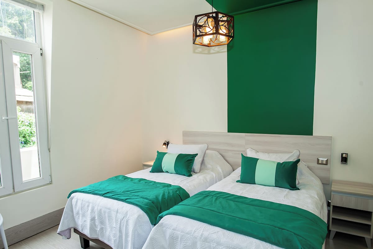 Quarto com duas camas, uma parede de destaque verde e um lustre.
