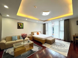 Quarto de hotel moderno com cama, sofá, mesa de centro e uma janela grande com cortinas.