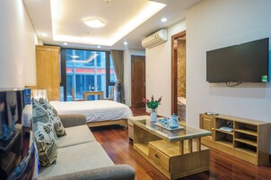 Quarto de hotel moderno com cama, sofá, televisão e mobiliário de madeira.