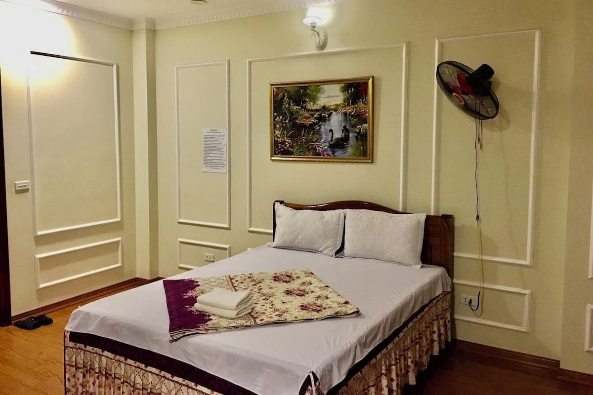 Quarto bem arrumado com cama, um quadro na parede e um ventilador.
