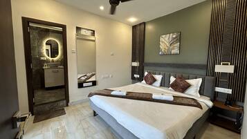 Quarto de hotel moderno com uma cama grande, ventoinha no teto, banheiro com espelho e pia, e um painel decorativo na parede.