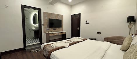 Quarto de hotel moderno com uma cama grande, uma televisão montada na parede, uma mesa com cadeira e um ventilador de teto.