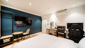 Quarto de hotel moderno com uma cama grande, uma escrivaninha com computador, uma TV na parede e uma cadeira.