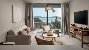 Sala moderna com sofá, poltronas, televisão e vista para a água.