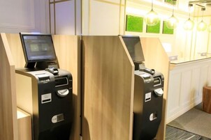 Uma área de recepção de hotel com dois balcões de madeira, cada um equipado com um computador e uma máquina registradora.