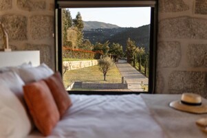 Quarto com parede de pedra e janela com vista para um vinhedo.