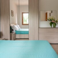 Quarto com cama, penteadeira, mesa de cabeceira, janela e espelho.