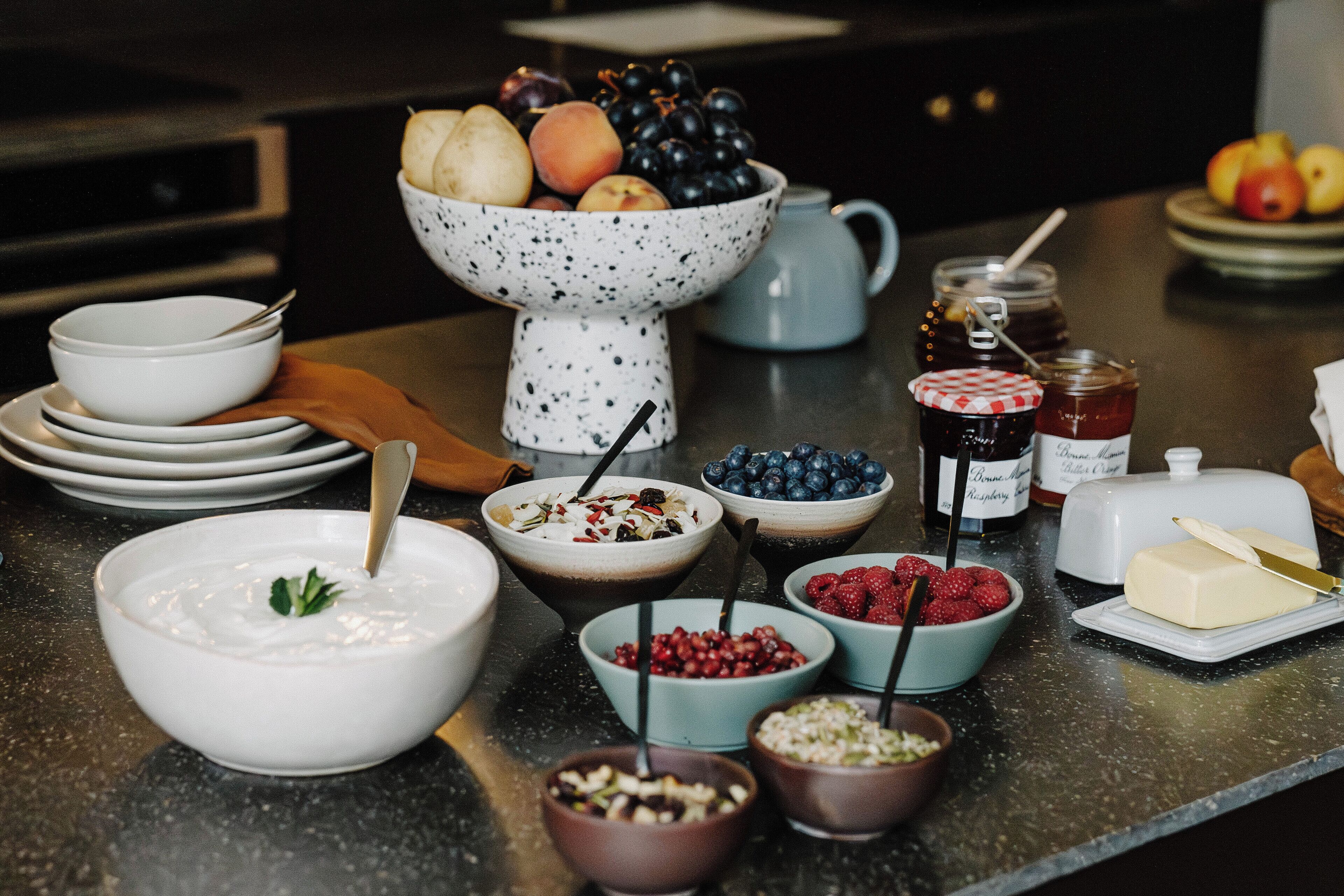 Uma bancada de cozinha com diversas tigelas de comida, incluindo frutas, iogurte e nozes.