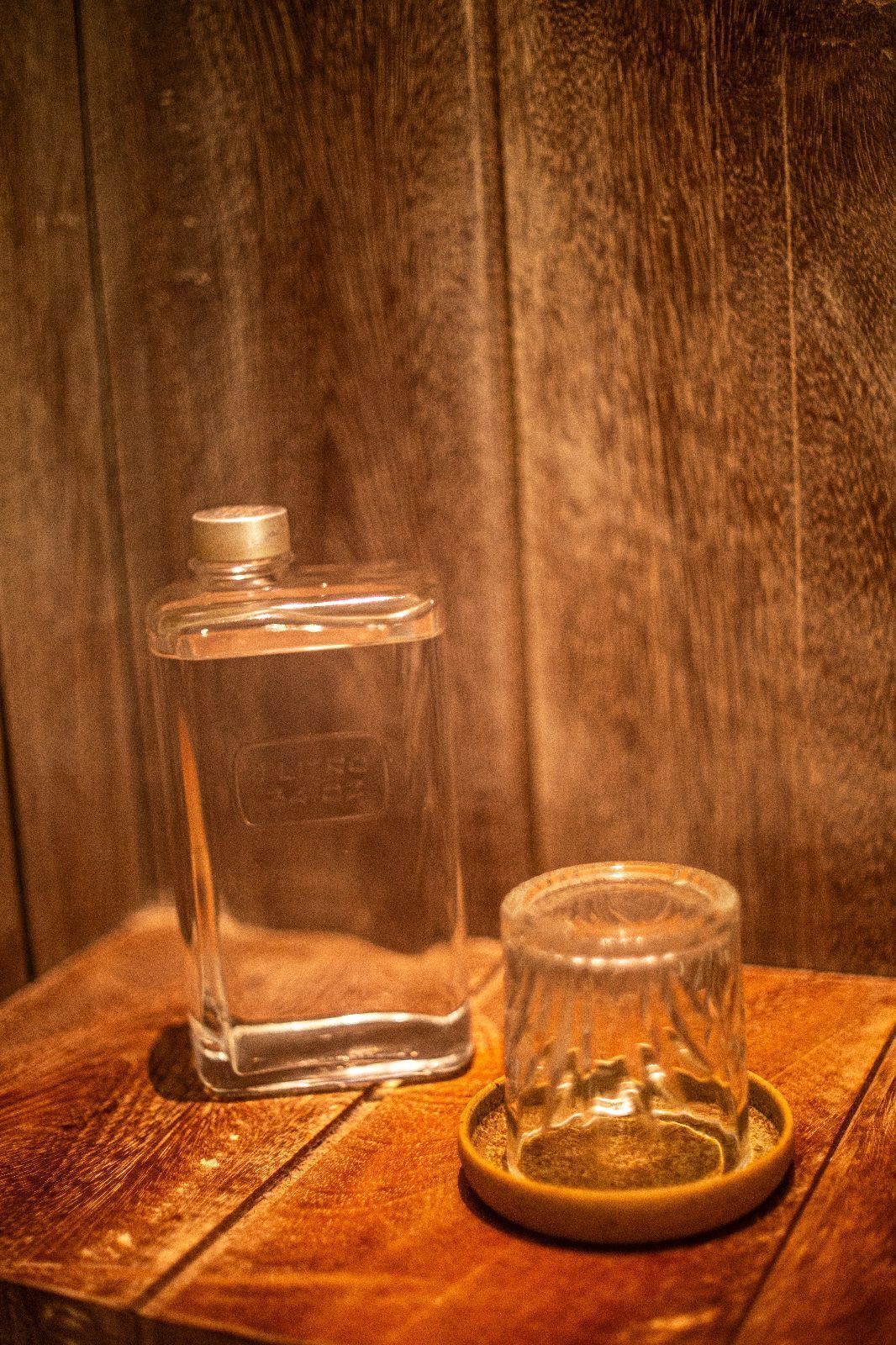 Uma garrafa de vidro transparente e um copo sobre uma superfície de madeira.