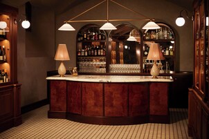 Uma área de bar com balcão curvo de madeira, duas lâmpadas e um espelho exibindo garrafas e copos.