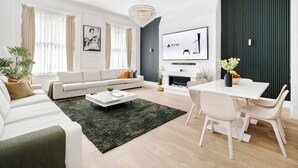 Uma sala de estar moderna com um sofá branco, uma mesa de jantar com cadeiras, uma lareira e uma grande tela de televisão.