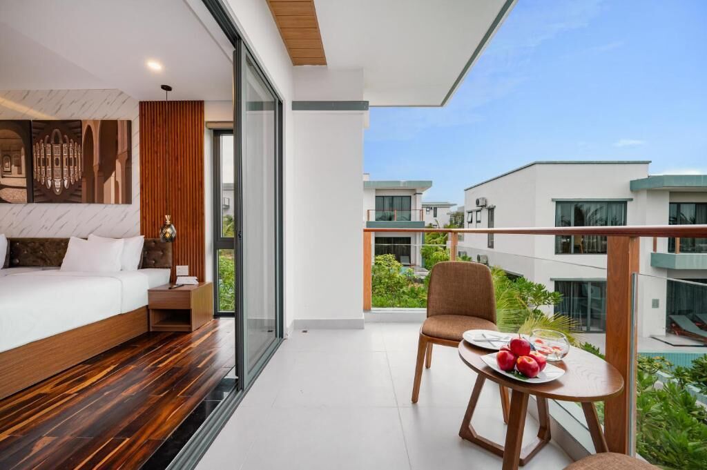 Varanda moderna com sofá branco, mesa de madeira com frutas e vista para edifícios próximos.
