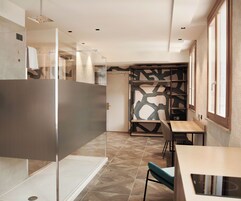 Quarto de hotel moderno com divisória de vidro, secretária de madeira e parede estampada.