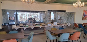 Um restaurante com balcão de mármore, cadeiras coloridas e um candelabro.