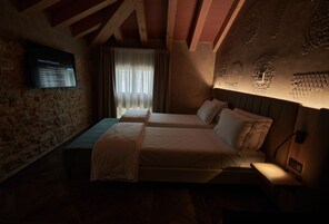 Um quarto com pouca luz, duas camas, uma parede de pedra e uma tela fixada exibindo texto.