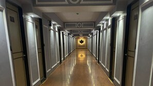 Um corredor comprido e estreito, com piso de madeira e portas em ambos os lados.