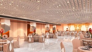 Uma ampla sala de banquetes com mesas e cadeiras redondas, teto estampado e iluminação acolhedora.