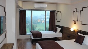 Quarto de hotel com duas camas, uma janela grande com cortinas, uma televisão de tela plana e um luminário fixado na parede.