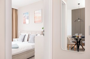 Quarto de hotel moderno com cama, mesa de cabeceira e área de refeições com mesa e cadeiras.