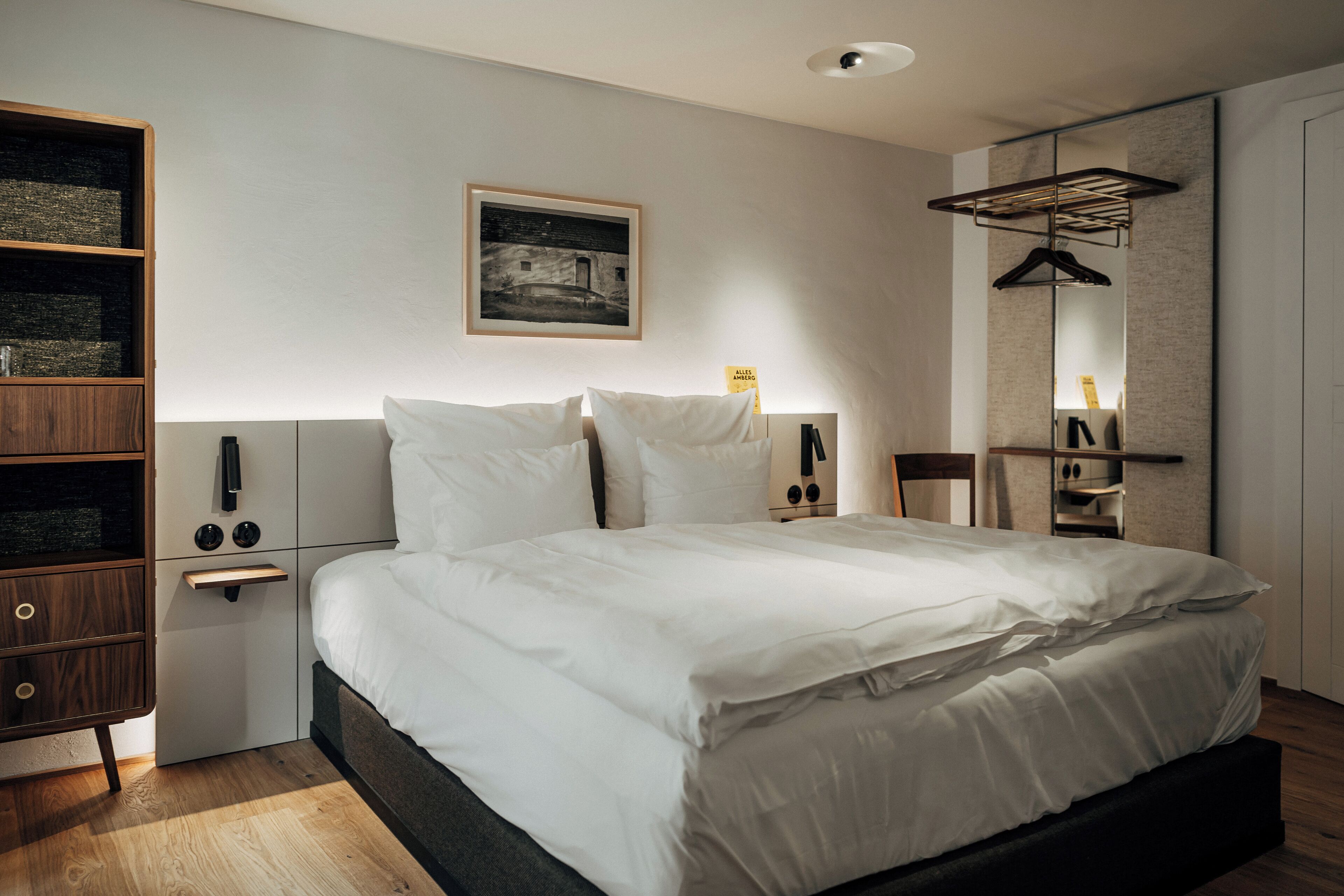 Quarto moderno com uma cama grande, uma mesa de cabeceira de madeira, uma estante, um quadro na parede e um lustre.