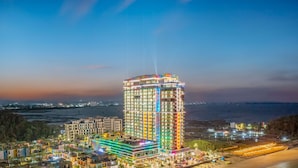 Um hotel moderno com vários andares, vista para a água e localização urbana bem iluminada.