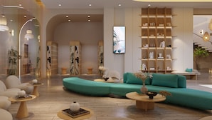 Uma sala de estar moderna com um sofá verde-água, poltronas bege e mesas de centro de madeira. Há uma estante com livros e objetos decorativos.