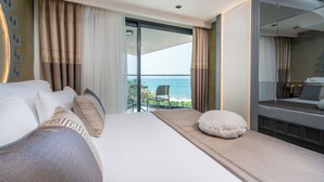 Quarto de hotel moderno com uma cama grande, uma varanda com vista para o mar e um espaço de estar separado com vista para o oceano.