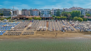 Uma praia com fileiras de espreguiçadeiras e guarda-sóis, um hotel ao fundo e céu claro.