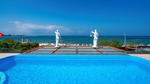 Piscina com vista clara para o oceano e duas estátuas.