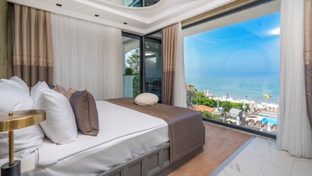 Quarto com uma cama grande, vista para o mar e varanda com mobiliário de exterior.