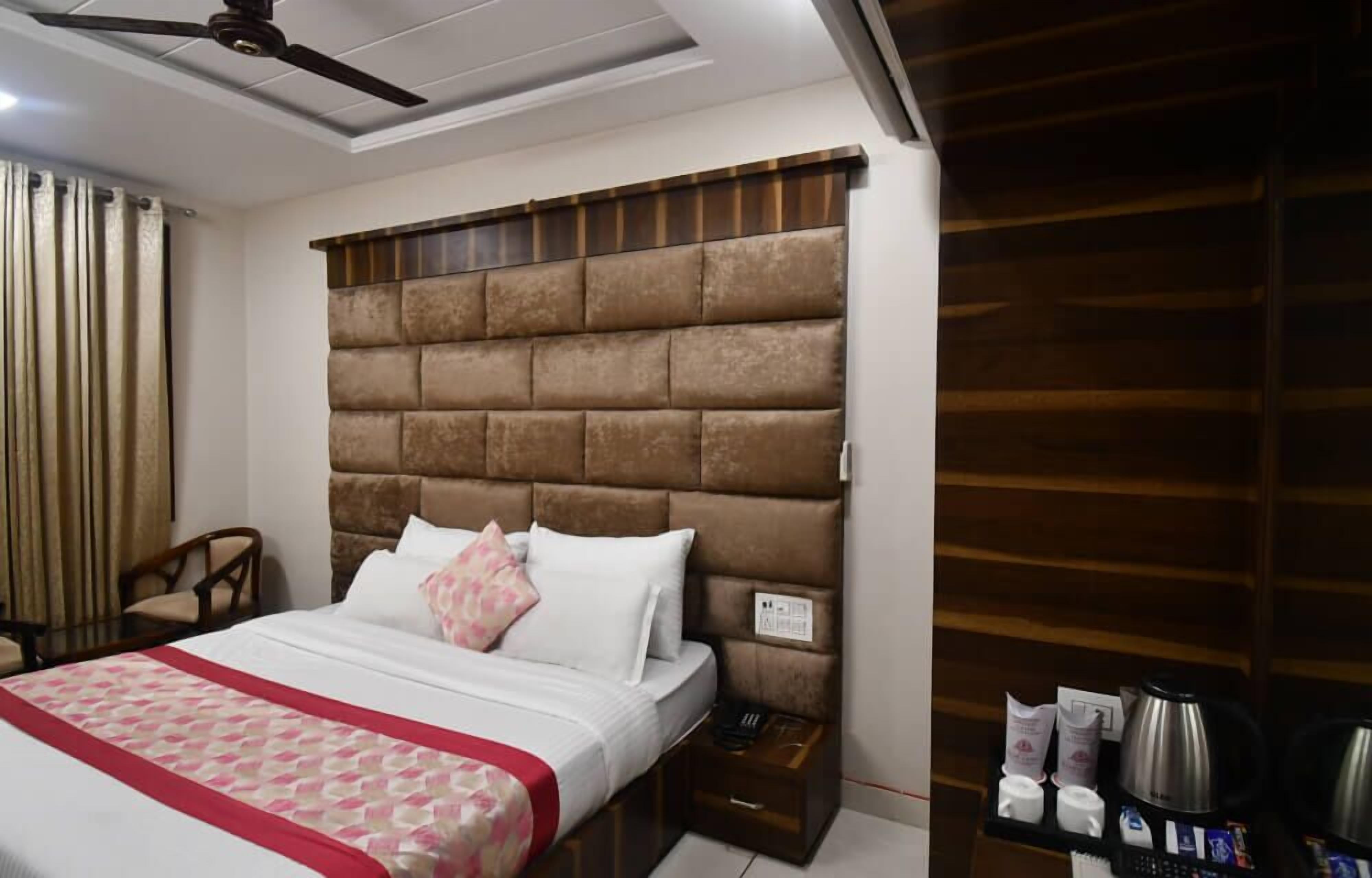 Quarto de hotel com uma cama grande, cabeceira, mesa de cabeceira, uma cadeira e um espaço para café.