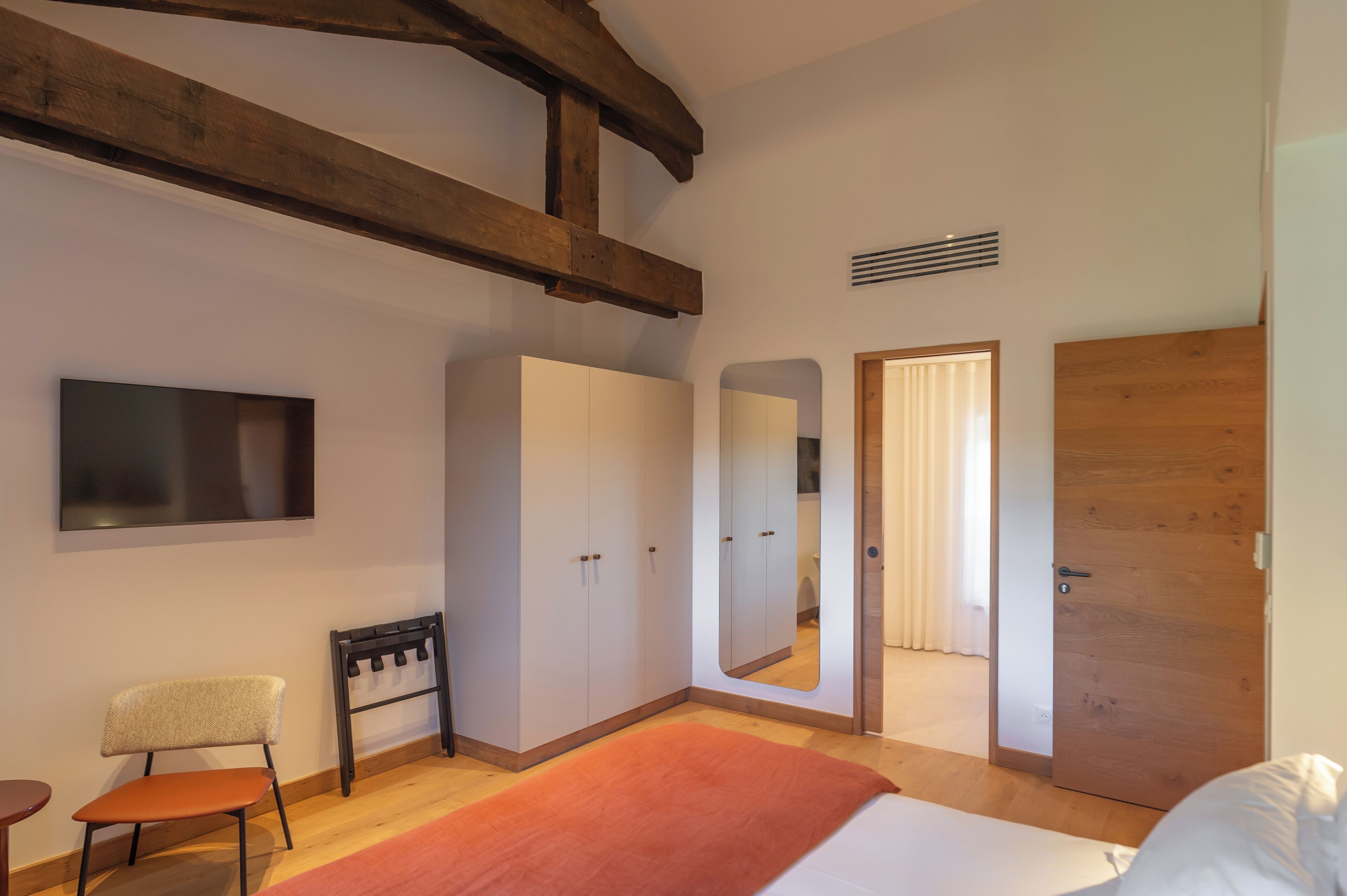 Um quarto com uma cama, um guarda-roupa, um espelho e uma cadeira.