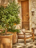 Uma porta de madeira, um vaso com planta e uma cadeira de madeira em ambiente externo.