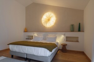 Quarto moderno com cama, mesas de cabeceira, luminária fixada na parede e estantes embutidas.