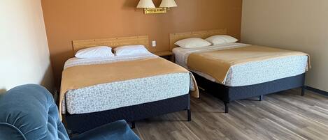Quarto de hotel com duas camas, uma mesa de cabeceira, uma luminária e uma cadeira azul.