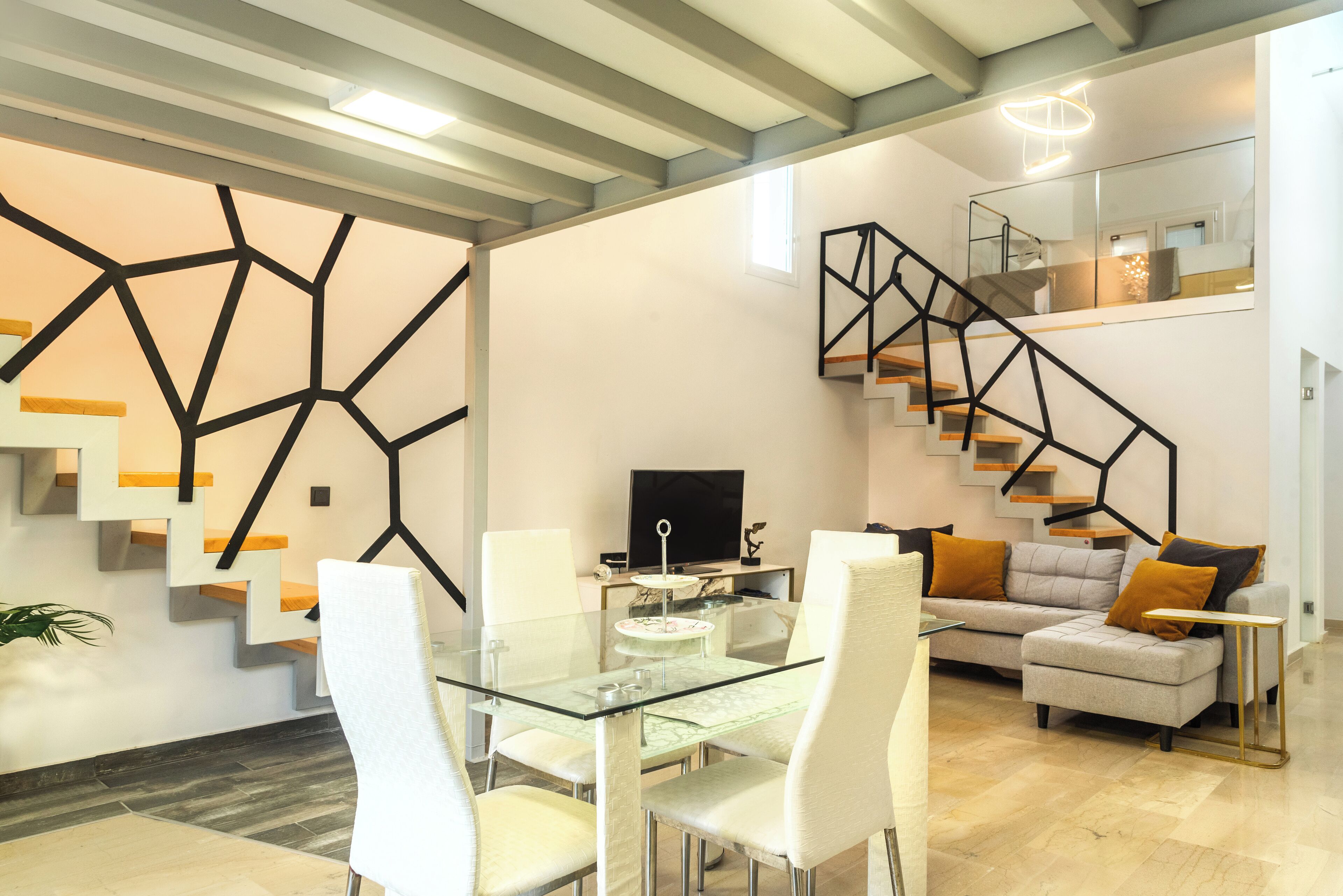 Uma sala de estar moderna com uma mesa de jantar de vidro, cadeiras brancas, um sofá cinza com almofadas laranja e um design geométrico na parede.