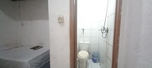 Quarto pequeno e compacto com uma cama de solteiro, sanitário e chuveiro.