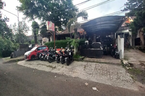 Um carro vermelho estacionado no acostamento de uma estrada, com várias motocicletas estacionadas em frente a um edifício.