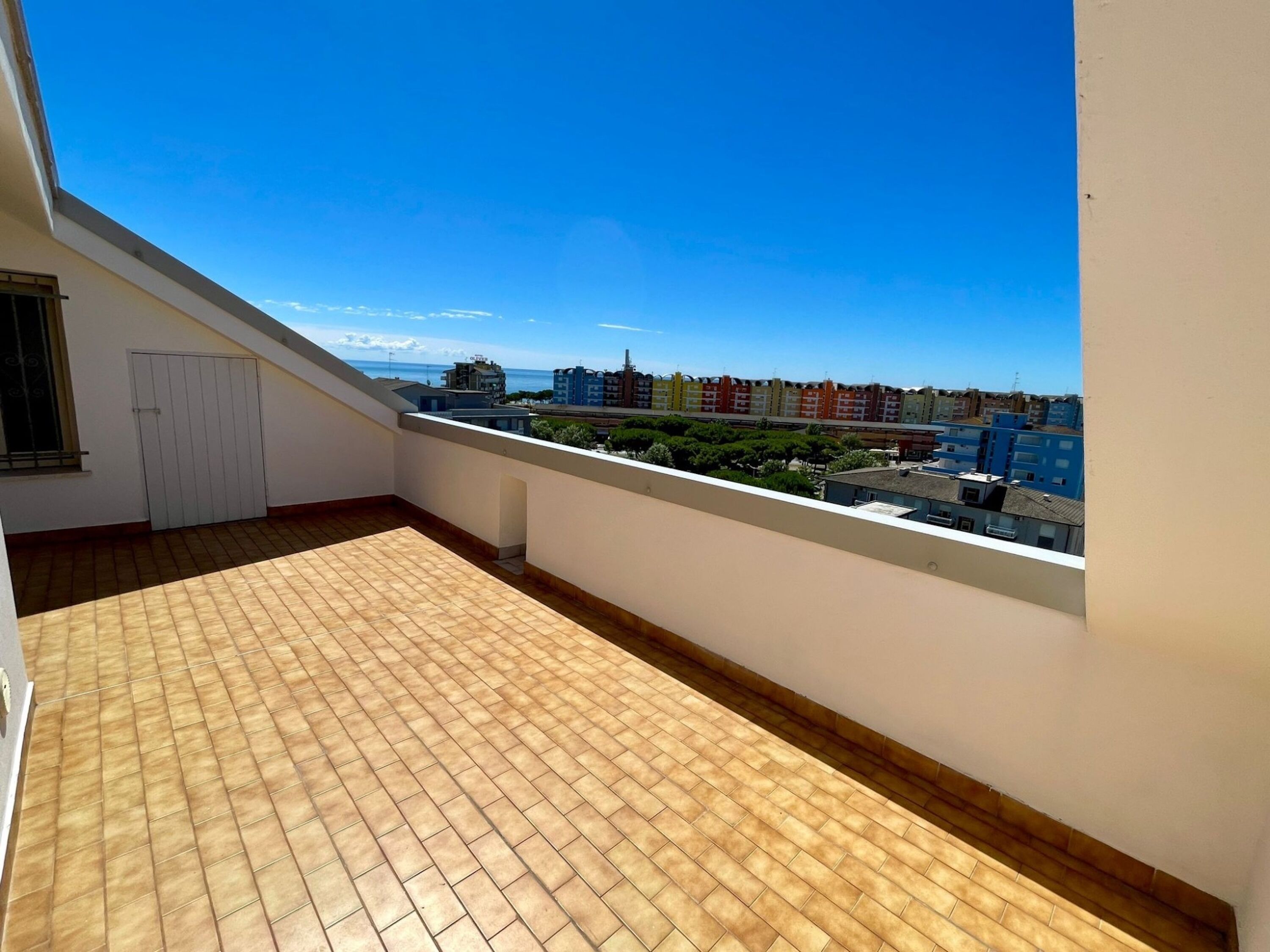 Terraço no telhado com chão de azulejos, uma porta branca e vista para um horizonte urbano com edifícios altos.