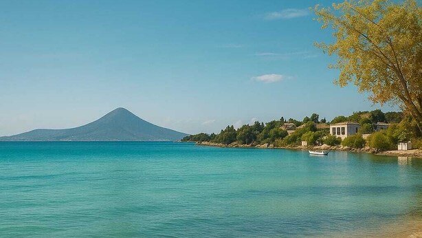 Uma praia com águas turquesa cristalinas, areia dourada e uma montanha ao fundo.
