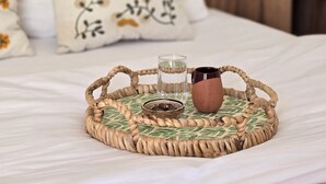 Cama com uma bandeja de vime que contém um copo de água, uma chávena e uma taça de azeitonas.
