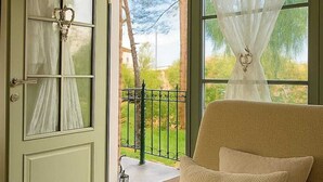 Um quarto com porta verde, sofá bege com almofadas estampadas, e vista para uma varanda com guarda-corpo.