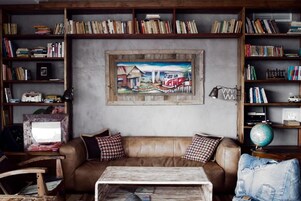 Uma sala de estar acolhedora com um sofá de couro marrom, uma mesa de centro e uma estante repleta de livros e um globo.